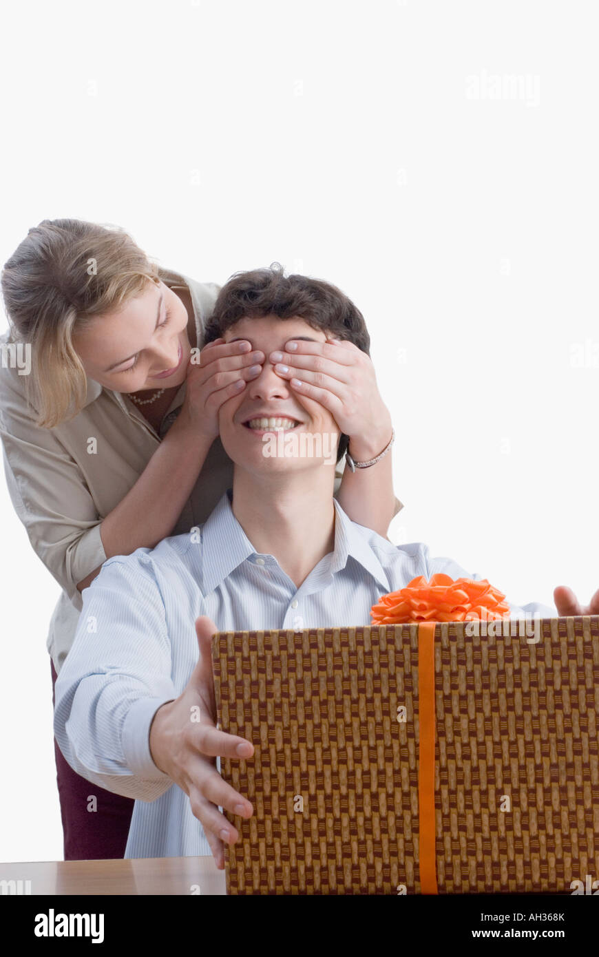 Close-up of a young woman covering a young man's eyes with a gift in ...
