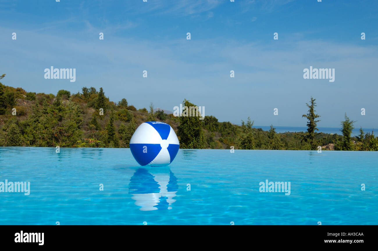 Infinity pool with floating inflated ball. View to sea over forested ...