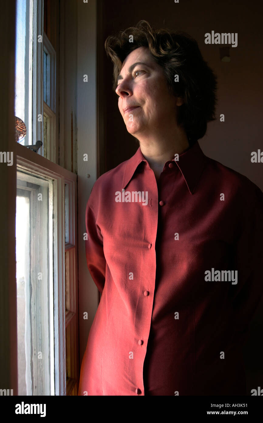 Middle aged woman gazing out a window in her house Model Released Stock ...