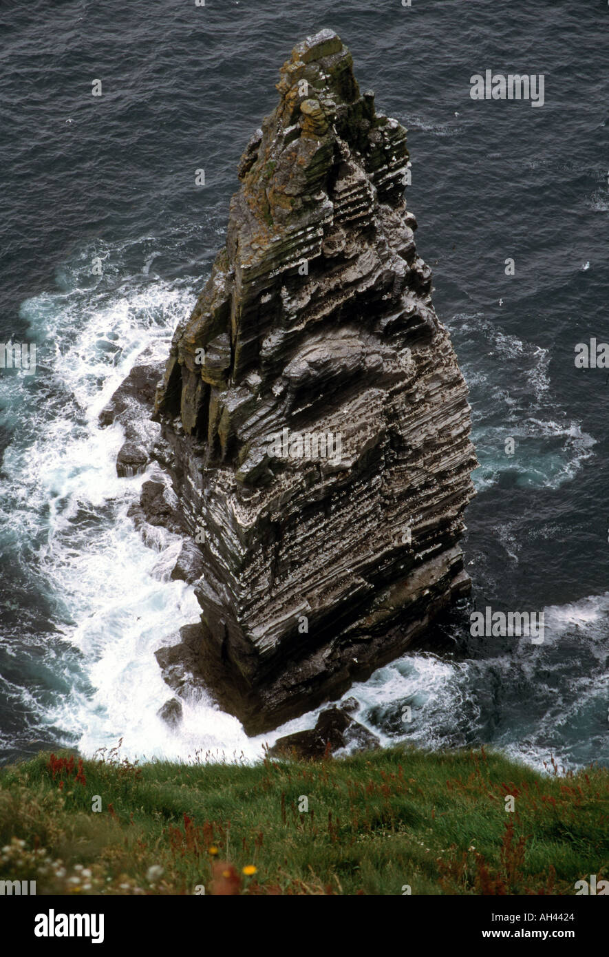 Large rock in form of a pyramid with frothy surf crashing around it off ...
