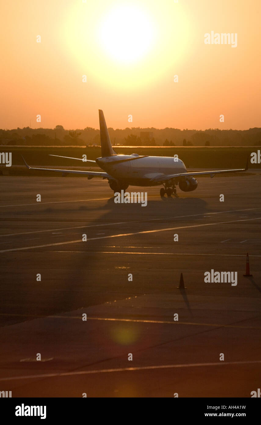 A lone commercial jet waits on a runway with the morning sun rising in ...