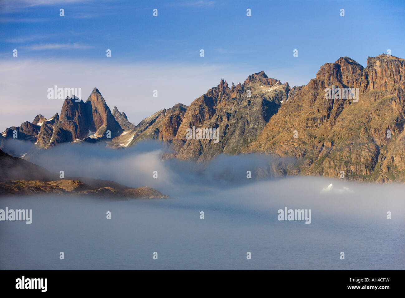 Rugged mountain peaks and small iceberg with wispy sea mist floating ...