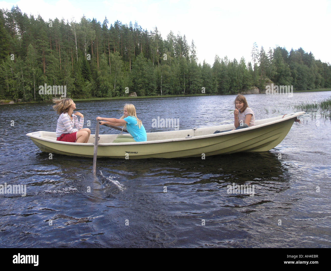 Three young girls in a rowing boat on lake Saimaa in Finland ...