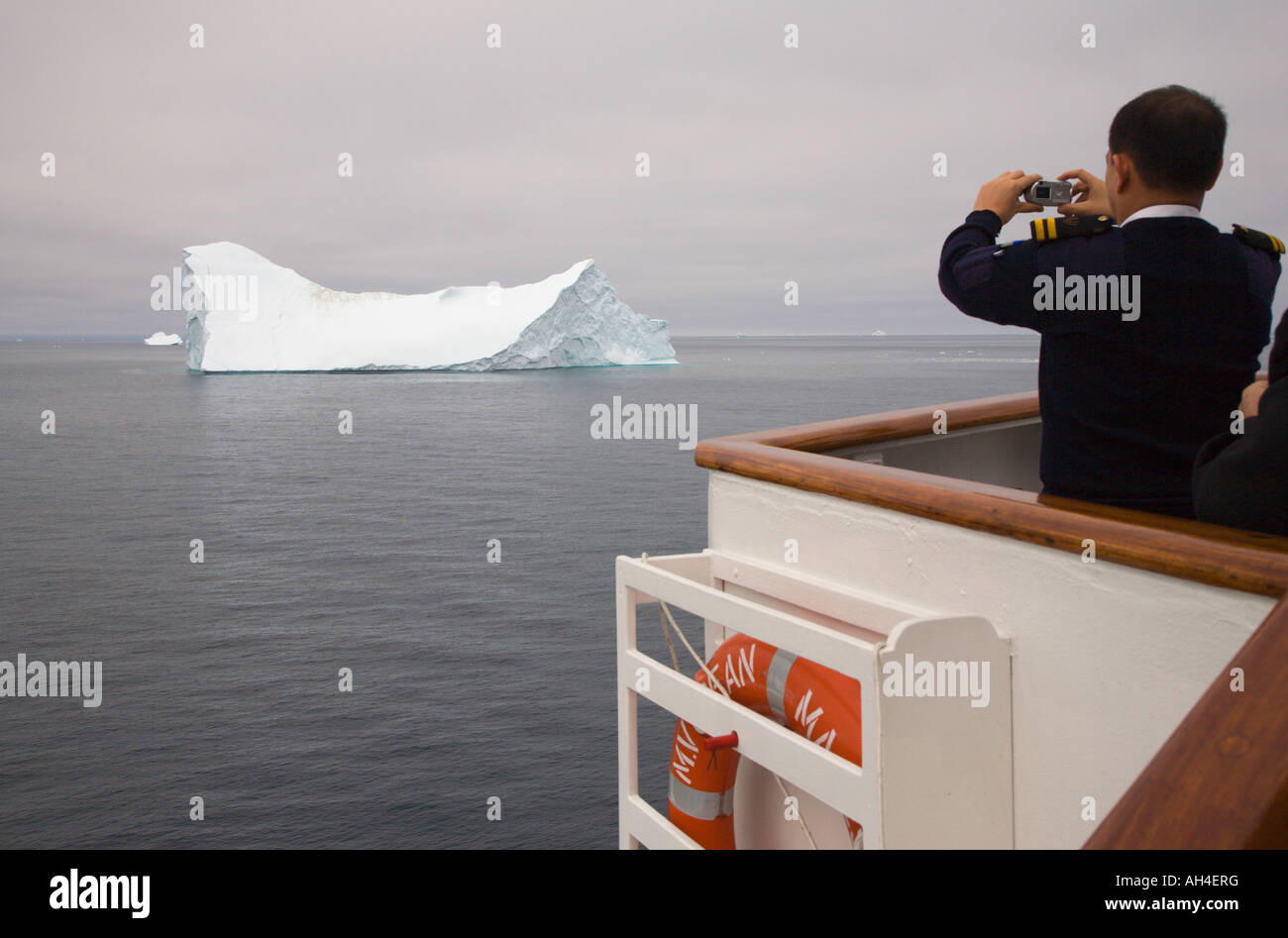 Officer on bridge of cruise ship taking photo of big iceberg passing on ...