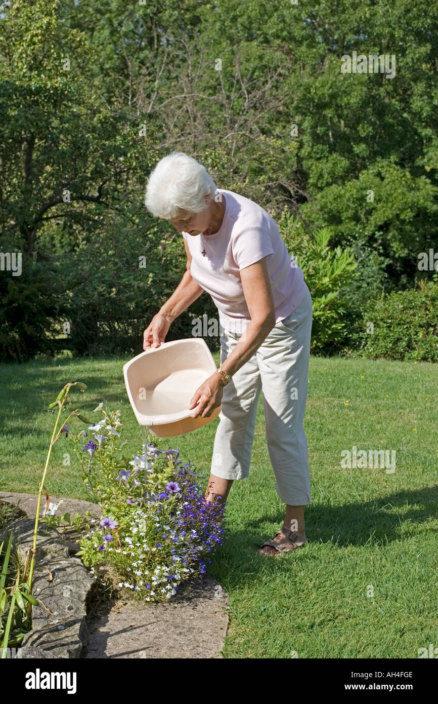 Woman using waste washing up water to water plants in garden Cotswolds ...