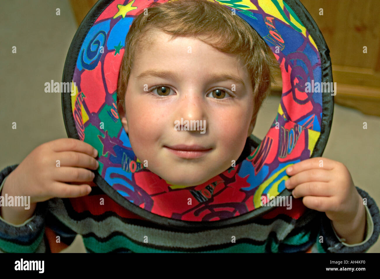 Attractive young boy child looking through a coloured ring toy and ...