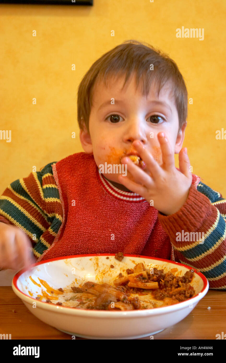 Young boy child with a bib eating pasta and mince with a spoon and ...