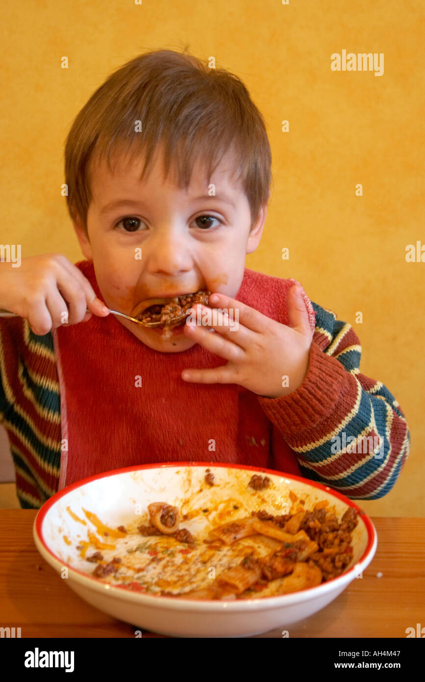Young boy child with a bib looking pleased eating pasta and mince with ...