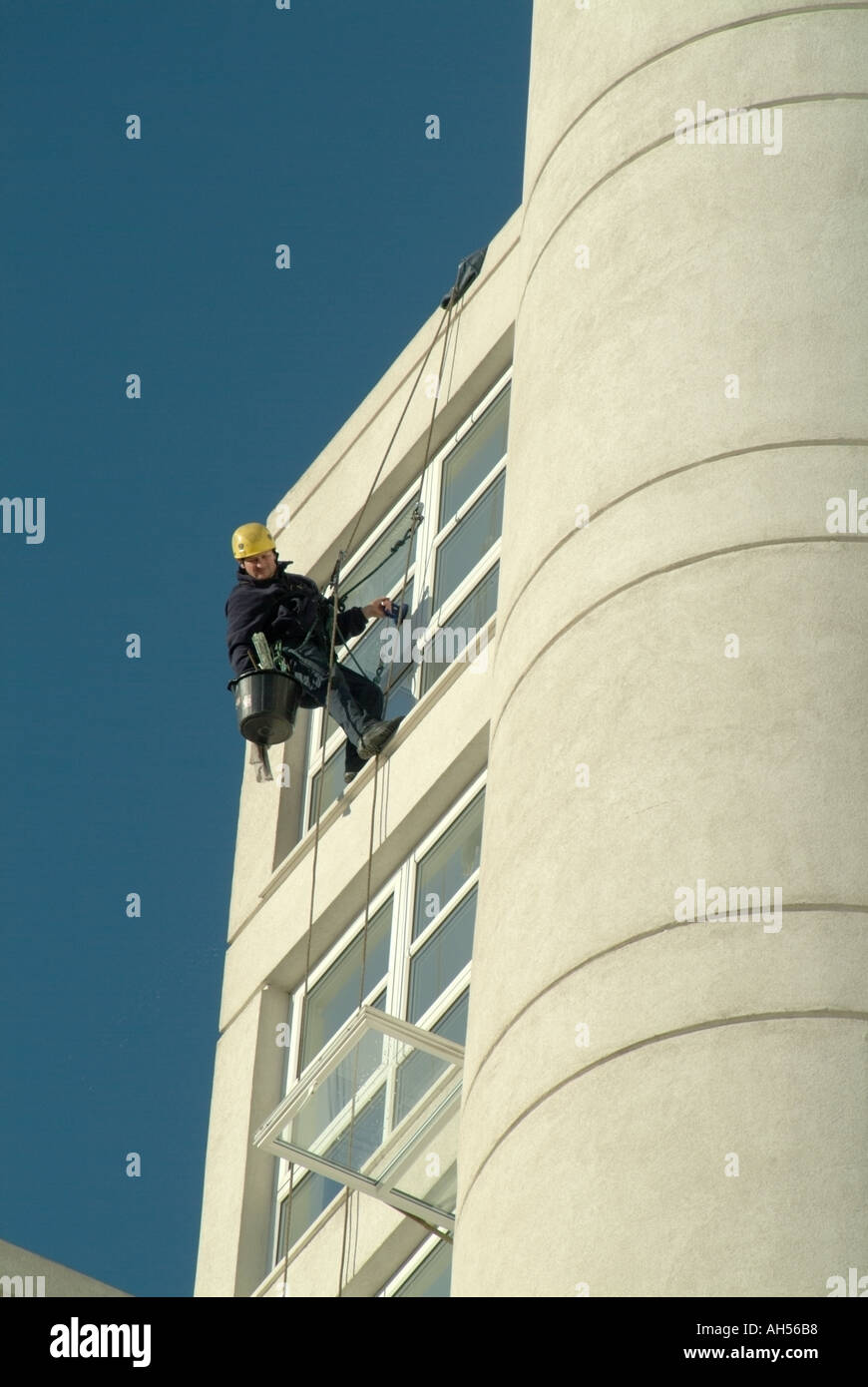 London Docklands window cleaner held in roped chair suspended from roof ...