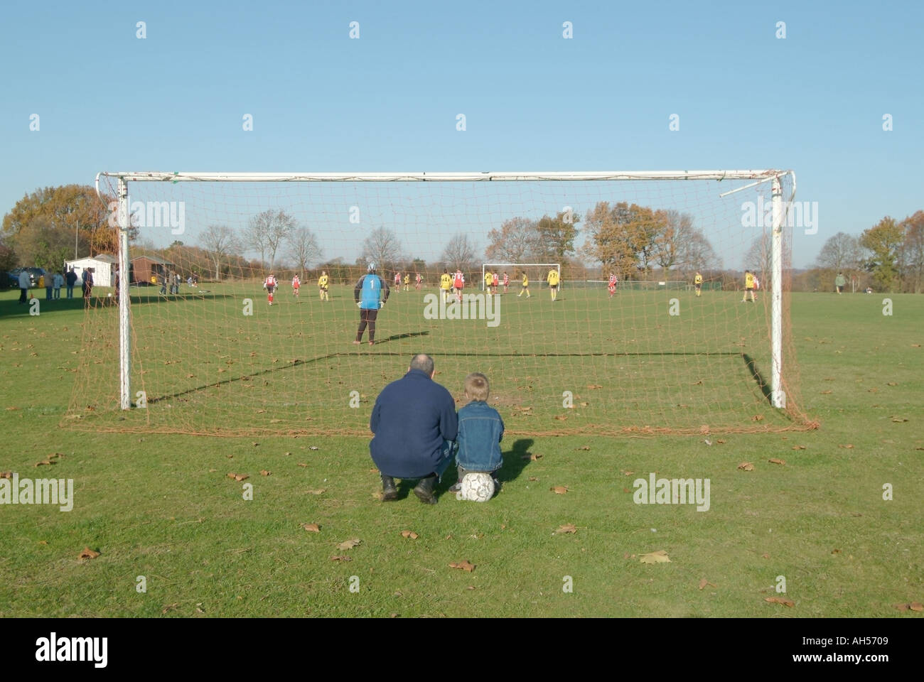 Father & young son & ball behind goal post watching teen kids playing ...