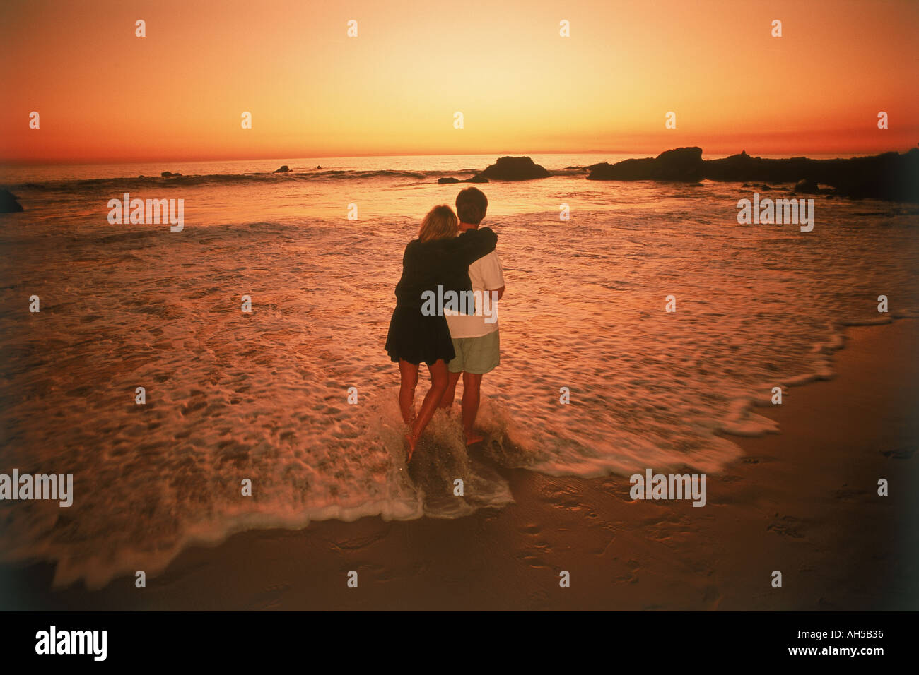 Couple enjoying romantic moments in waves breaking on sandy shore along ...