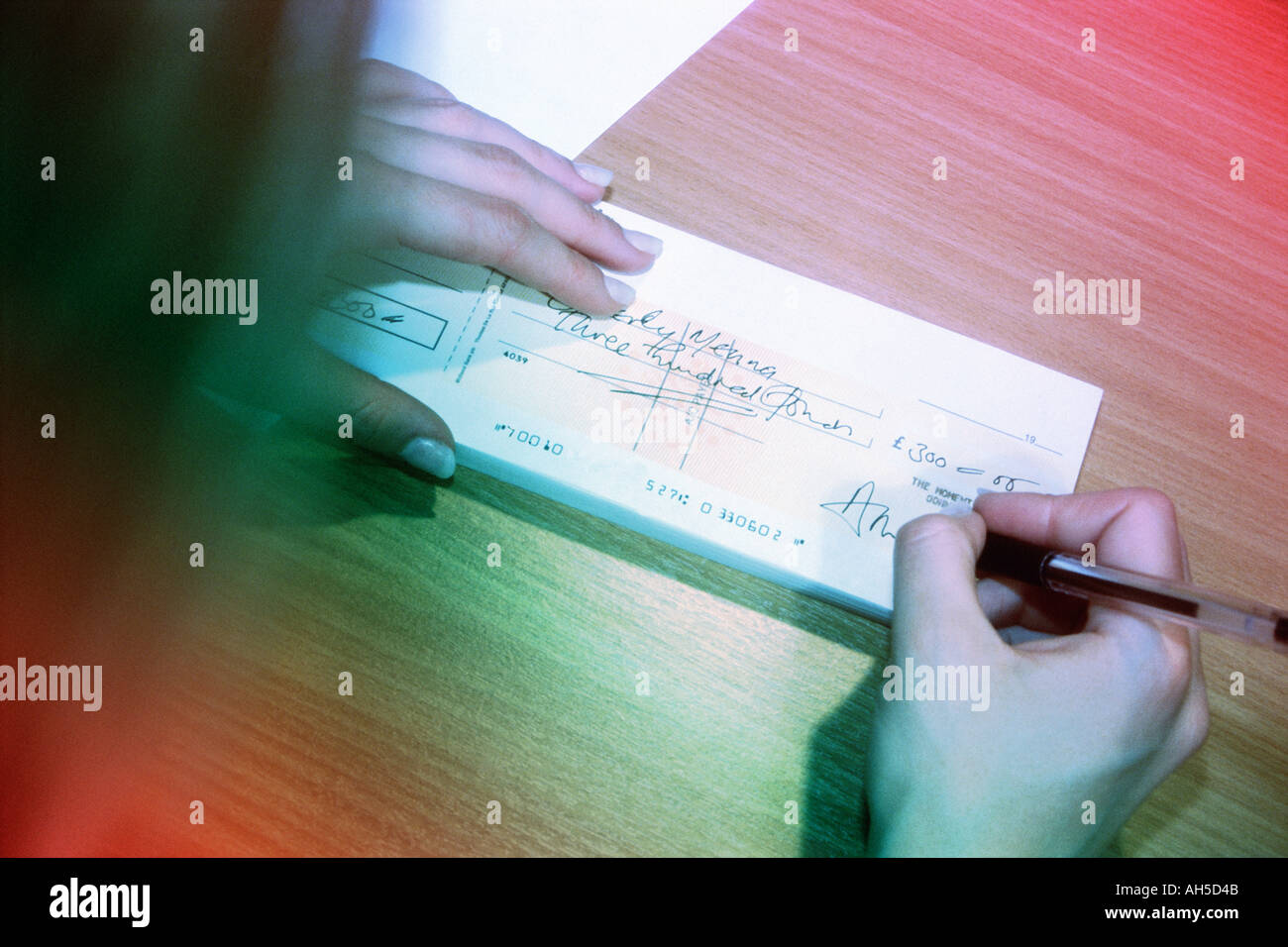 Female hand signing cheque book with pen at desk with soft lighting ...