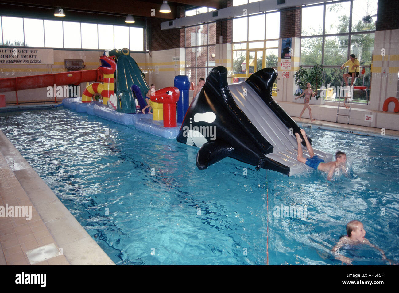 Children using water slide in swimming pool with lifeguard in ...