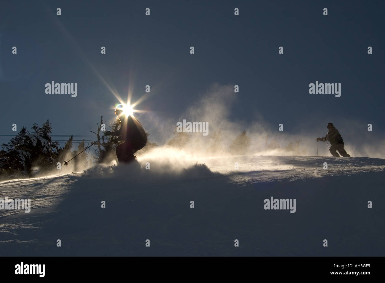 Two skies kick up powder snow as they are back lit on their way down a ...
