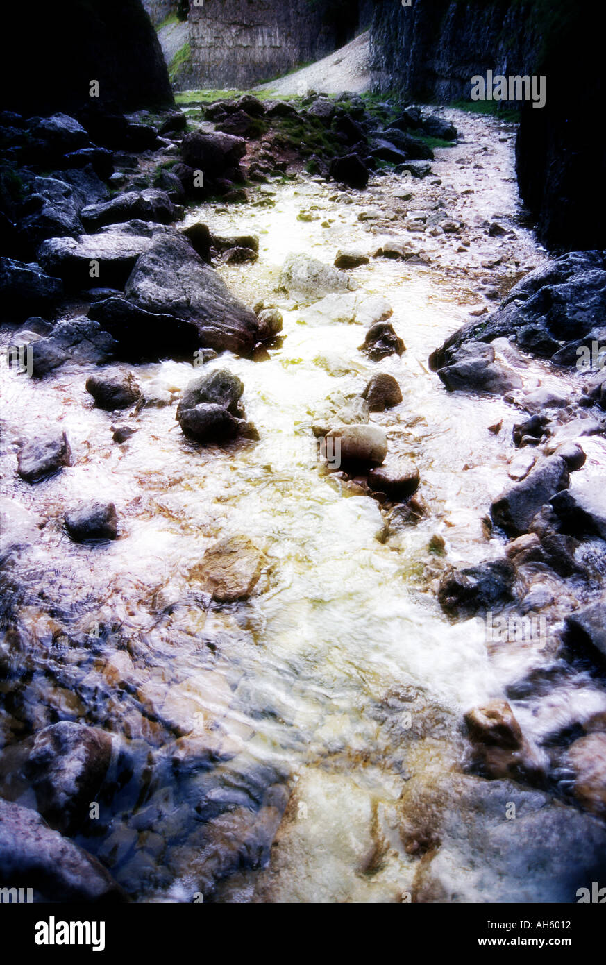 Water gushing down narrow gully with rocks and cliffs on either side ...