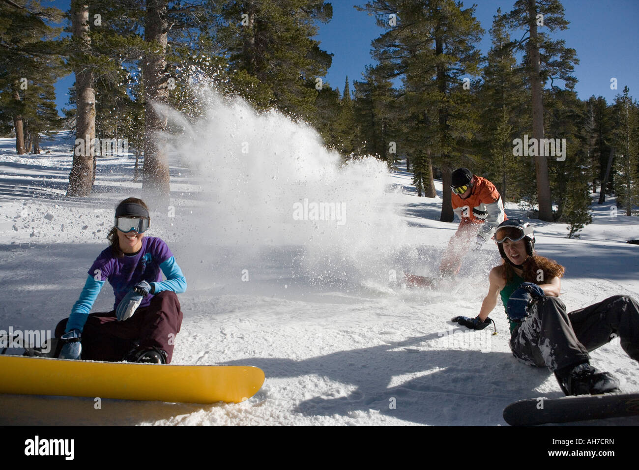 Two young women sitting on snow with a young man snowboarding behind ...