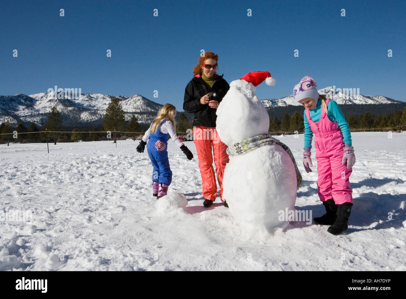 Mature woman with her two daughters building a snowman Stock Photo - Alamy