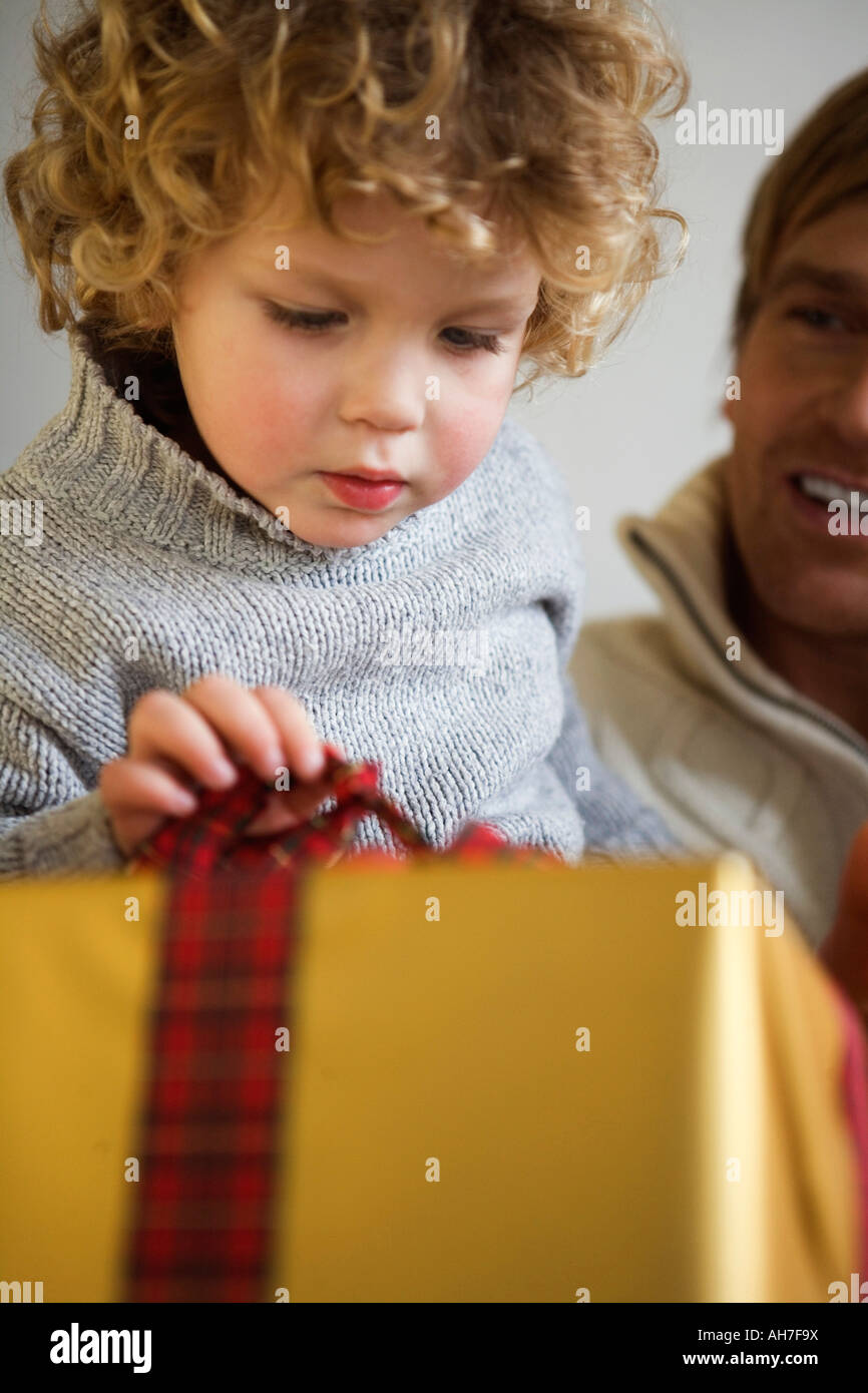 Close-up of a boy opening a Christmas present with his father behind ...