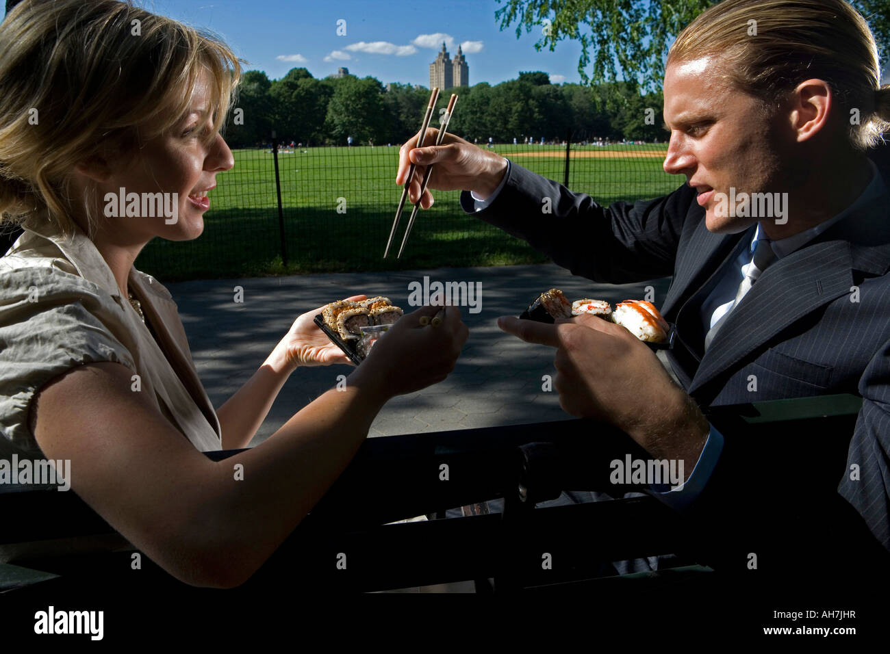 Young couple sitting on a park bench and eating sushi Stock Photo - Alamy
