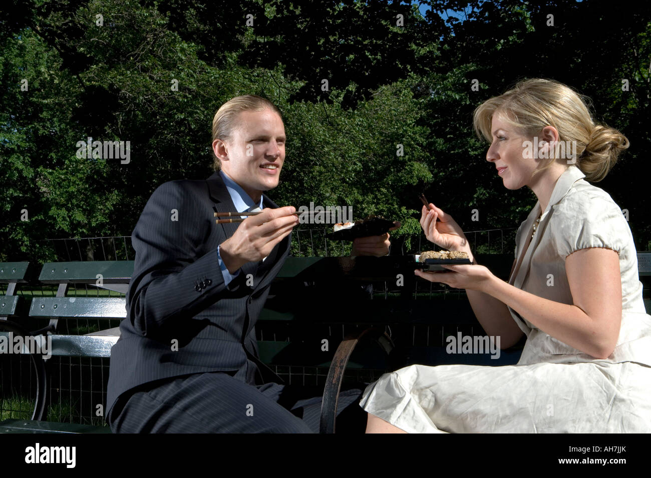 Young couple sitting on a park bench and eating sushi Stock Photo - Alamy