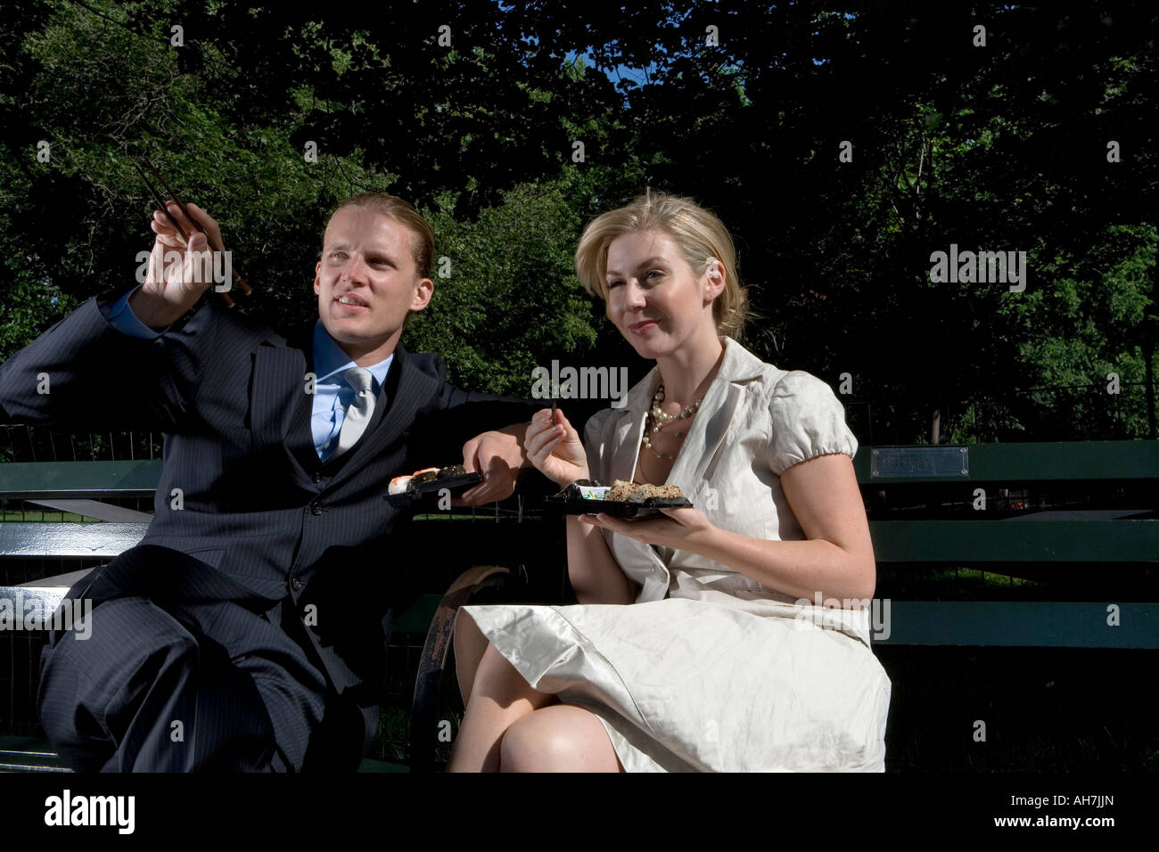 Young couple sitting on a park bench and eating sushi Stock Photo - Alamy
