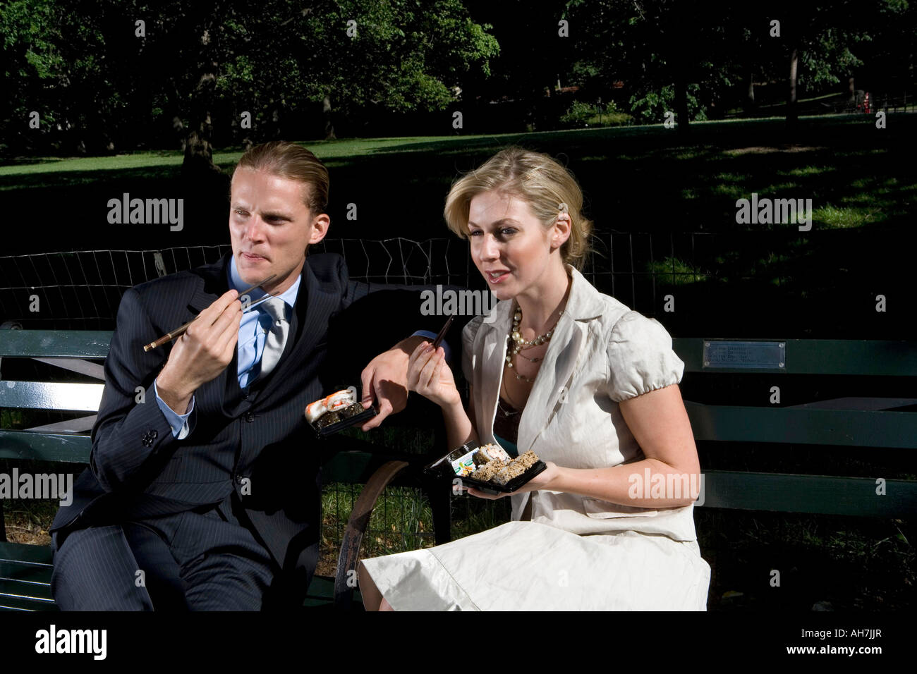 Young couple sitting on a park bench and eating sushi Stock Photo - Alamy