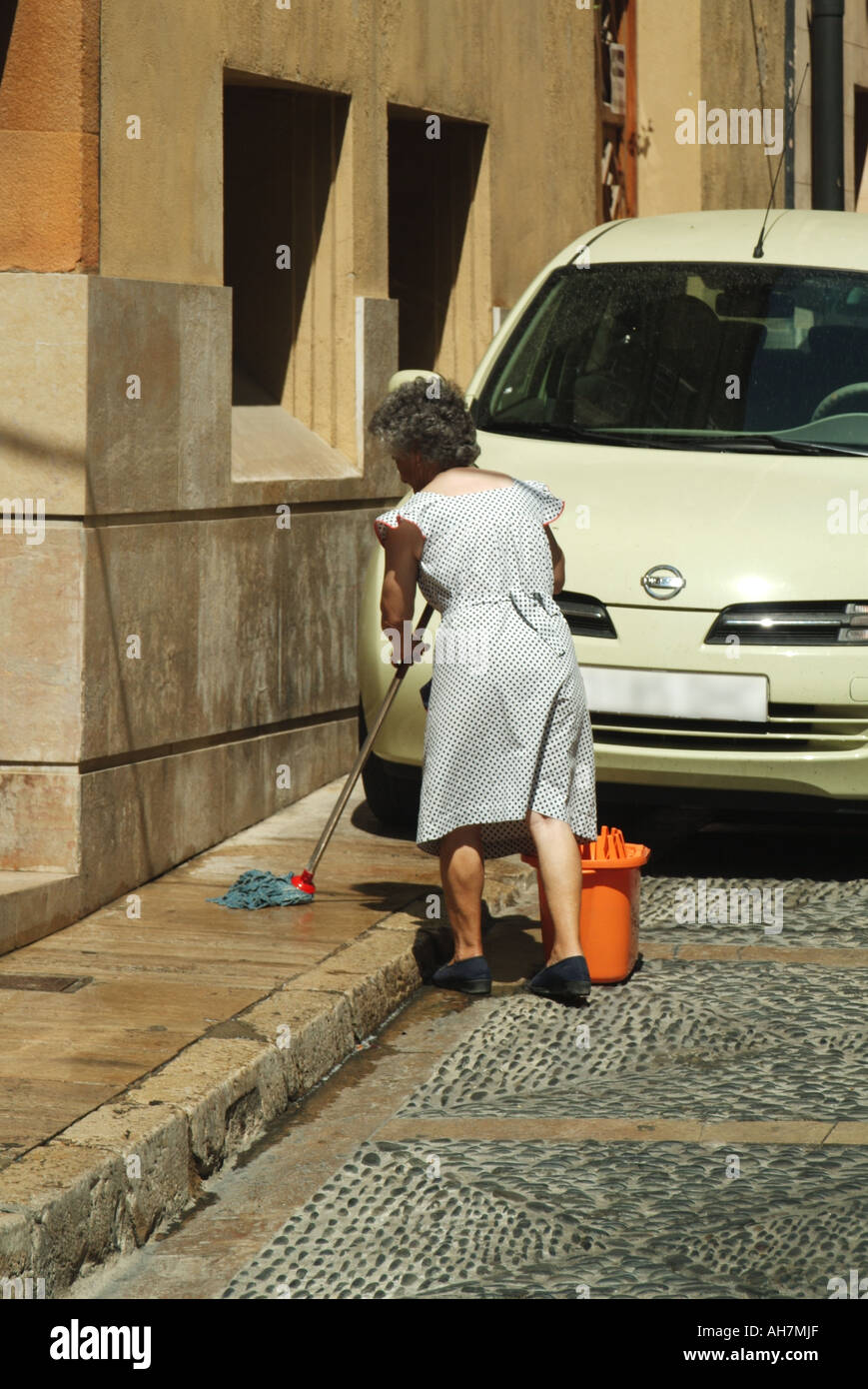 Tarragona woman with bucket and mop washing down the stone pavement and ...