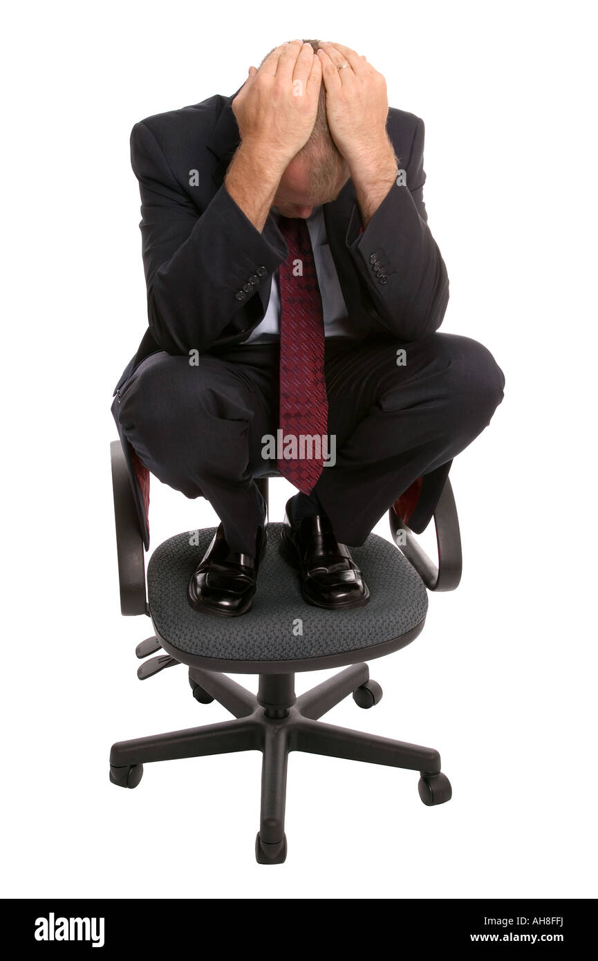 Businessman crouched on an office chair with his head in his hands ...
