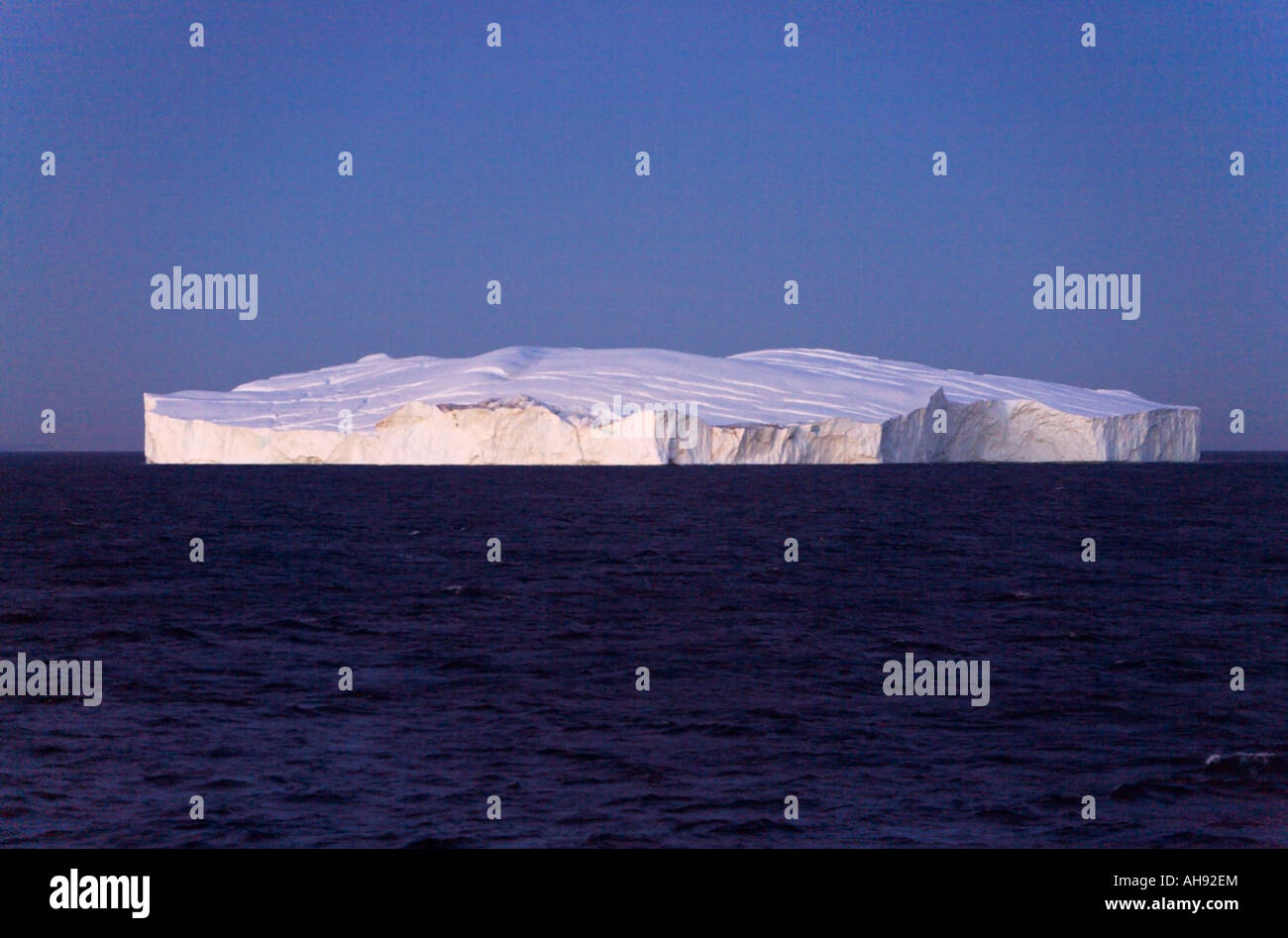Huge flat iceberg in early dawn light one side reflecting white in a ...