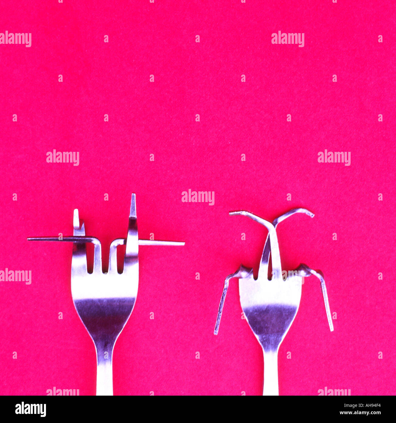 Two metal forks with teeth bent in to various shapes on strong pink red ...