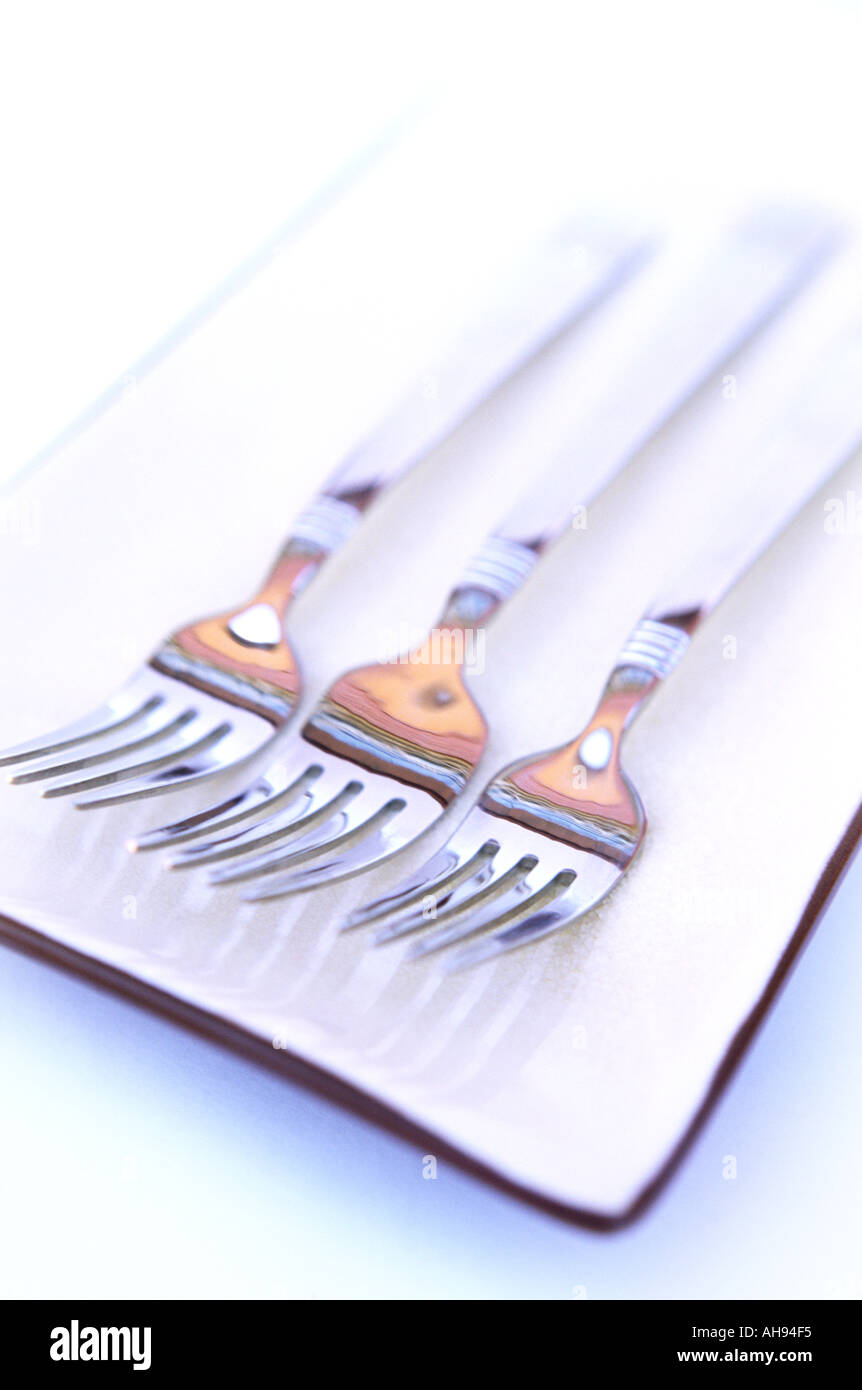 Three identical silver forks on an ornate rectangular plate on white ...
