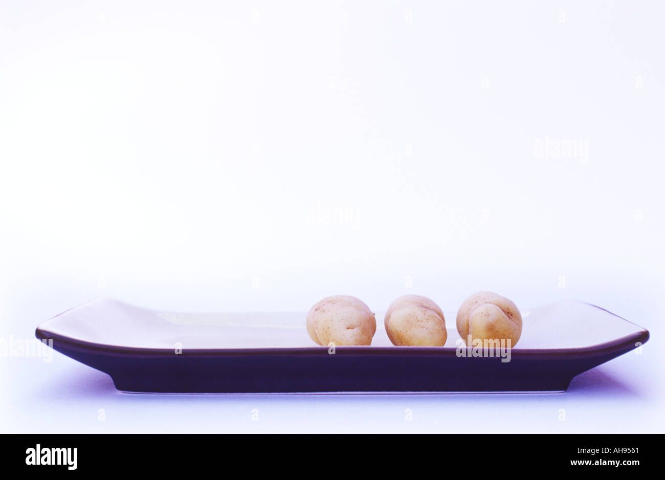 Three neat and clean potatoes on the end of a rectangular plate against ...