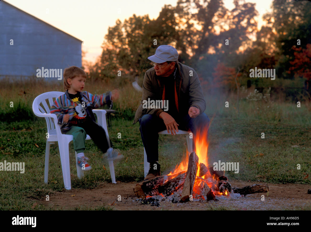 Boy child and grandfather sitting around campfire on family farm Stock ...