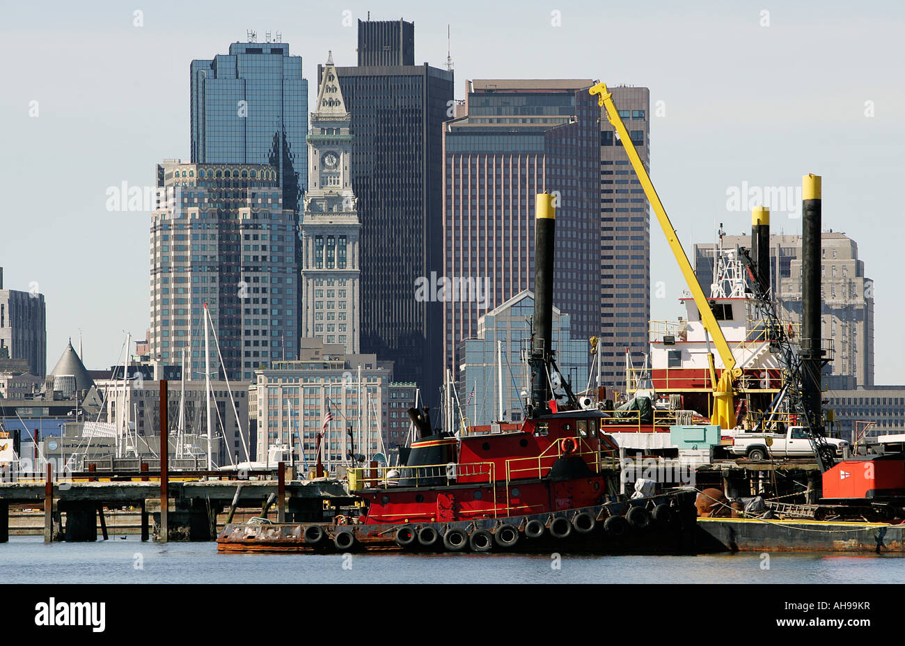 A red tugboat is tied to a dock in Boston Harbor with the city skyline ...