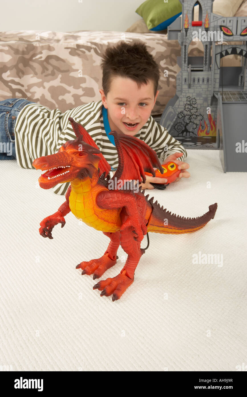 Boy lying down to play with remote controlled dragon in his bedroom ...