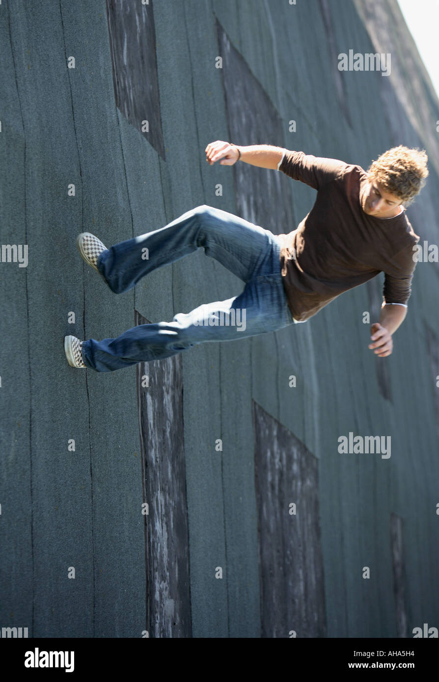 Vertical dramatic action portrait of young man jumping from wall ...