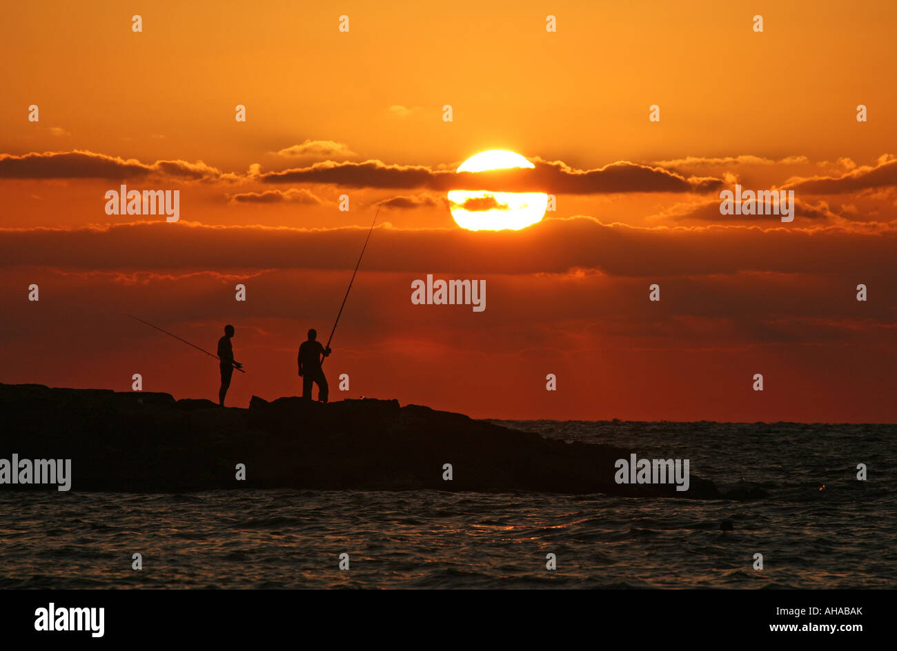 Two fishermen take in the sunset while fishing off a groin on the ...
