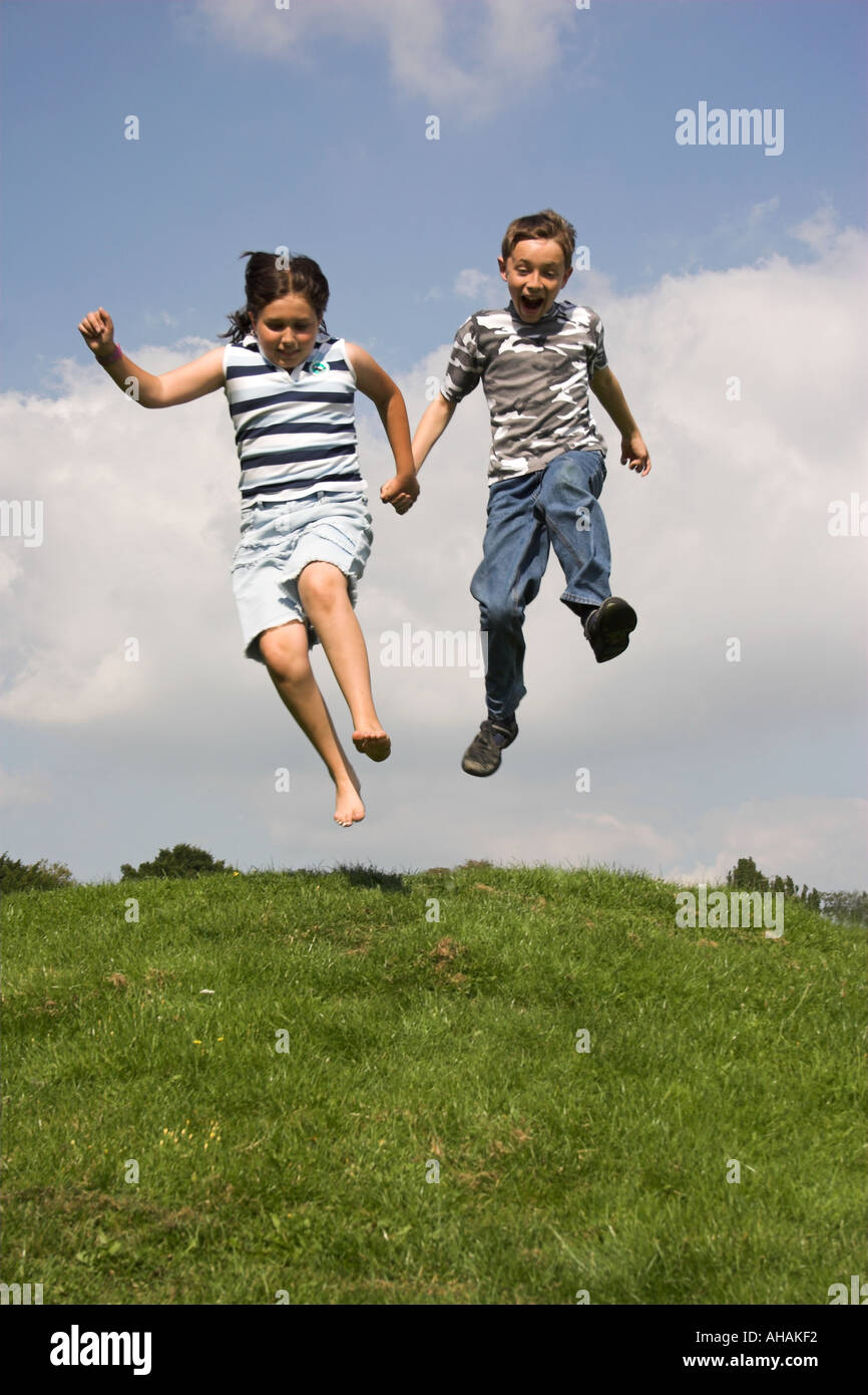 10 year old boy and girl running and jumping down a grassy bank Stock ...