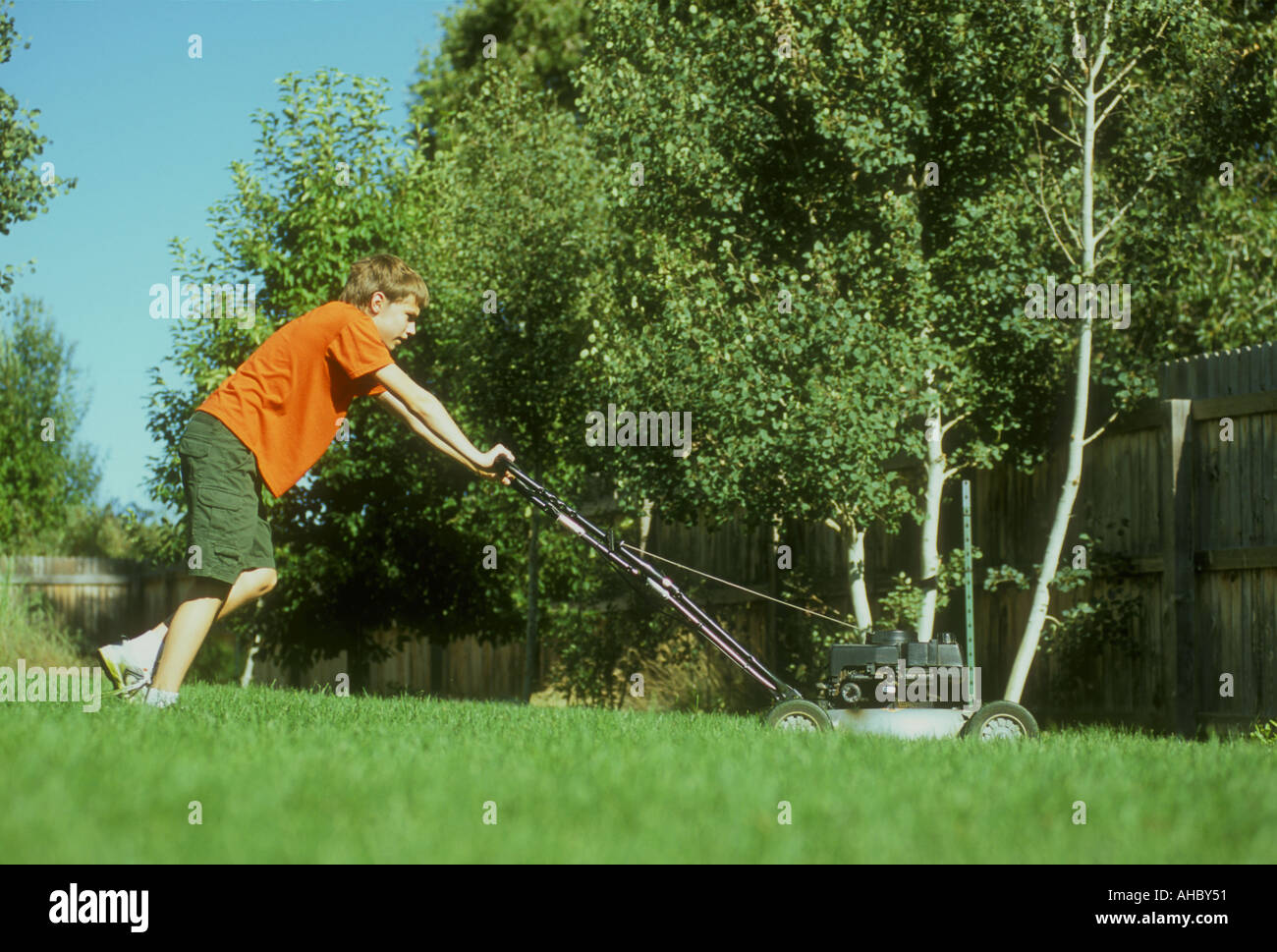 Young boy or man mowing a lawn with a power lawnmower Stock Photo - Alamy