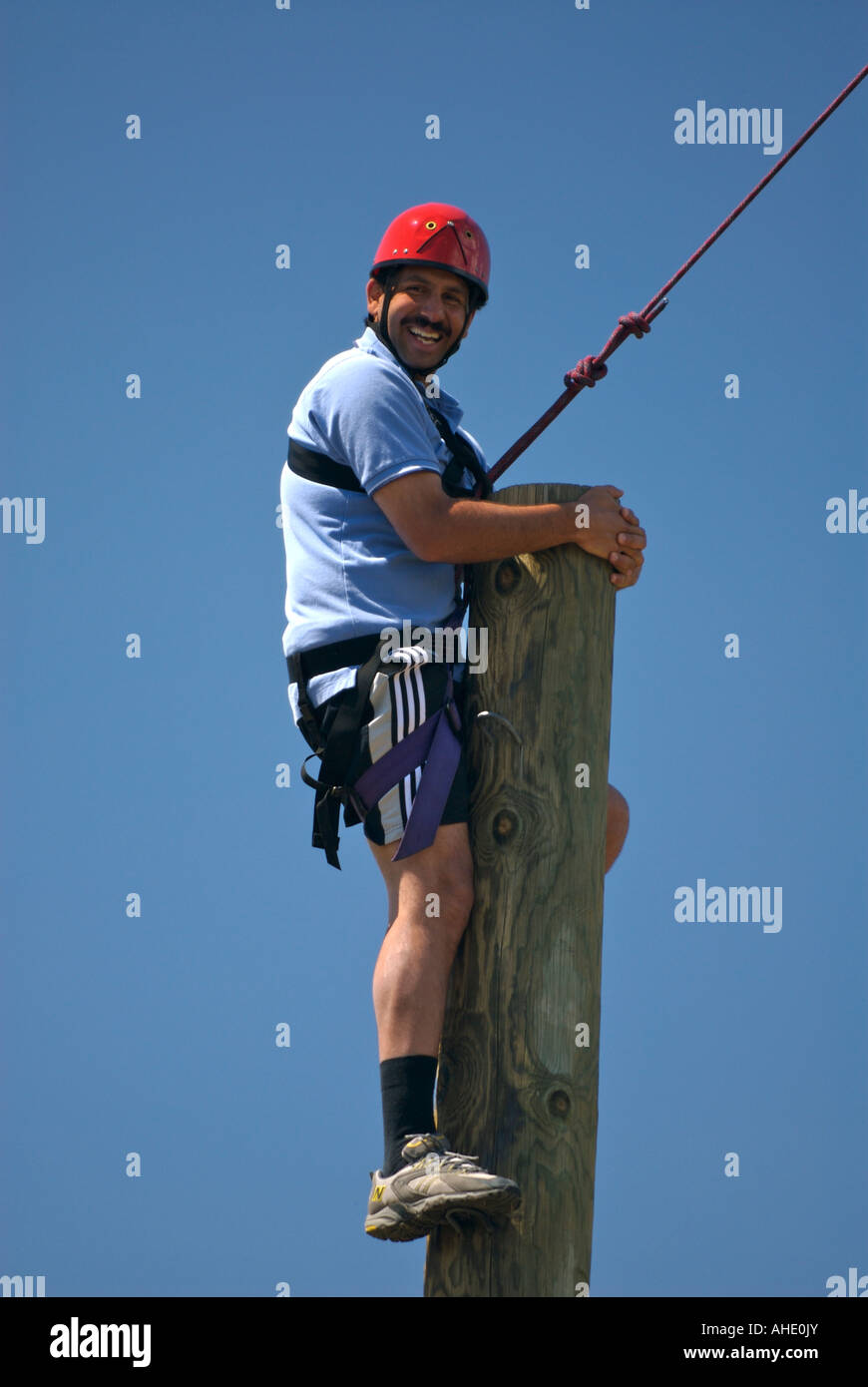 A smiling Pakistani man hugs a telephone pole as he climbs to the top ...