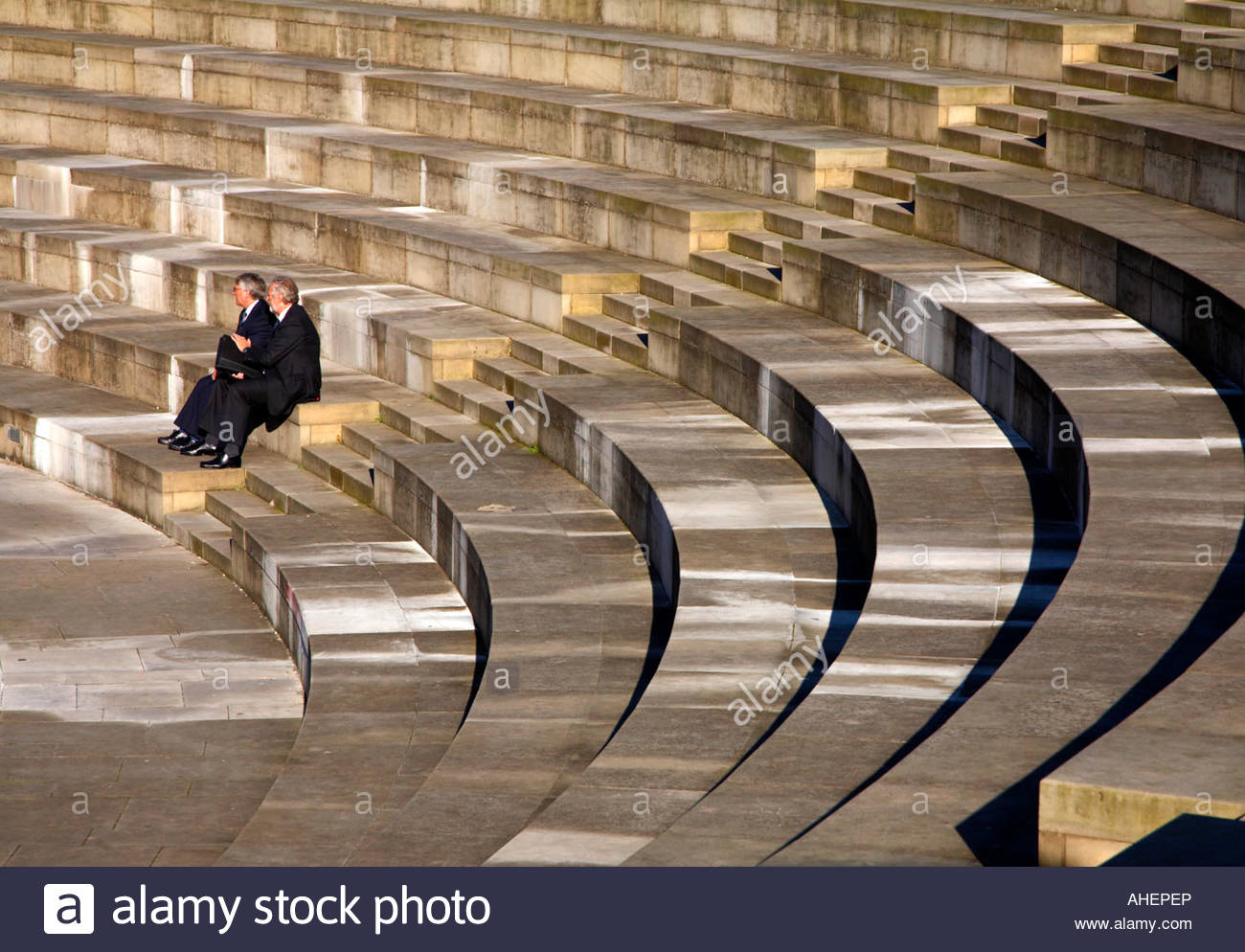 Two men in suits sitting on curved steps Stock Photo - Alamy