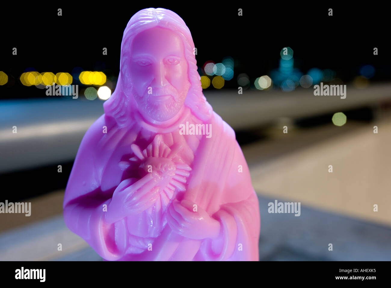 A pink statue of Jesus Christ stands alone against an urban street ...