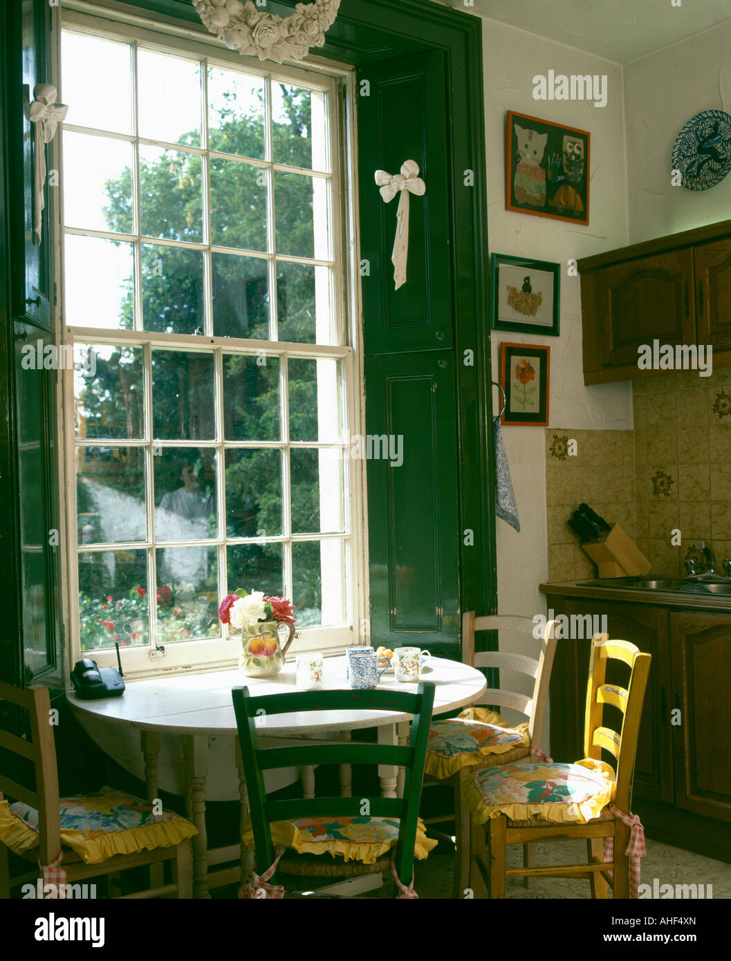 Table and chairs in front of sash window with green shutters in country ...