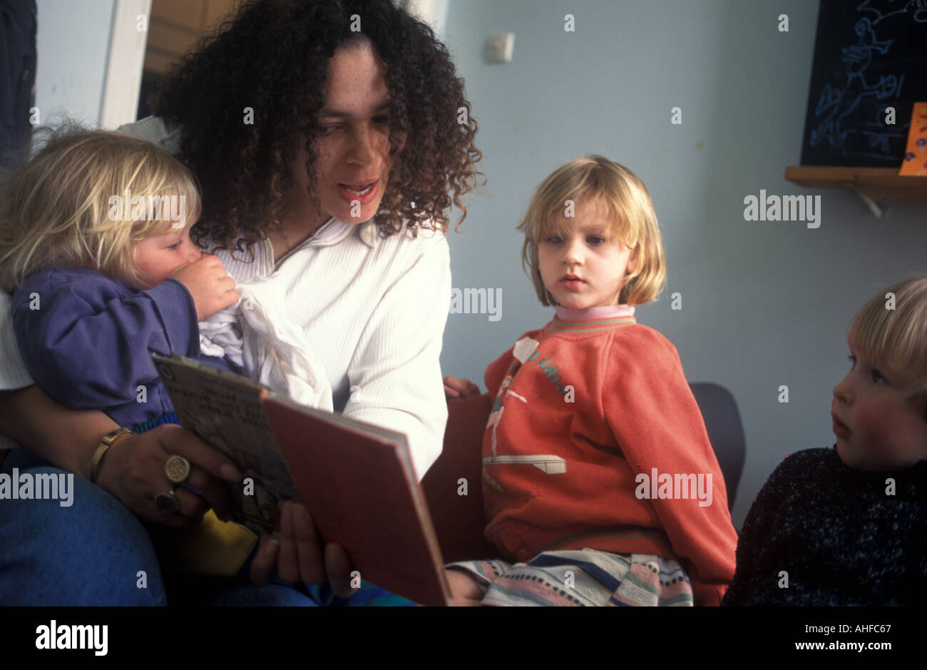 A child minder reading to three children at a creche, Hackney, London ...