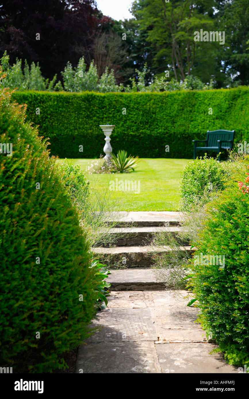 Stone steps to lawn with sundial in the centre and clipped hedge in the ...