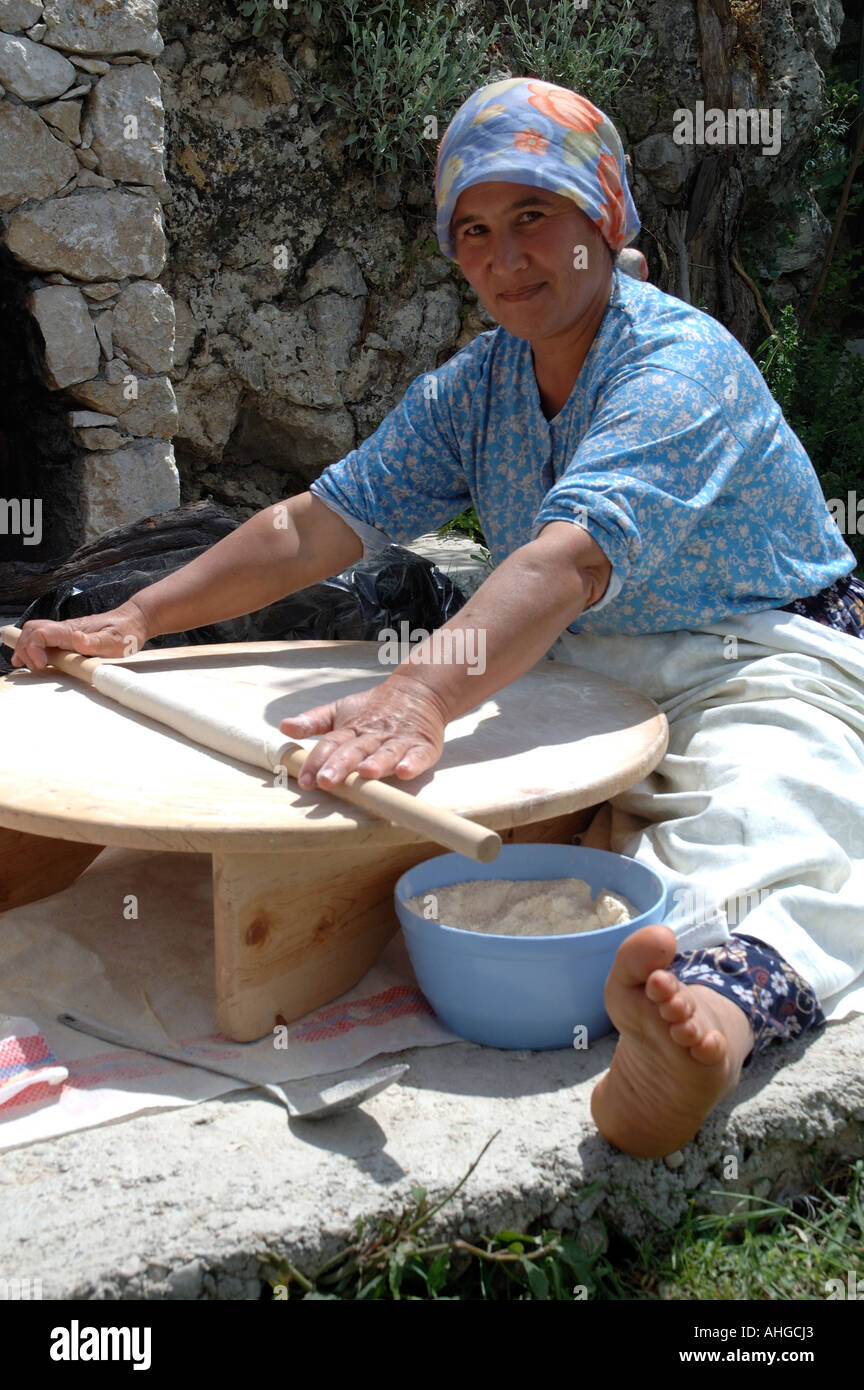 Woman making bread outdoors over open stone fire in rural village of ...