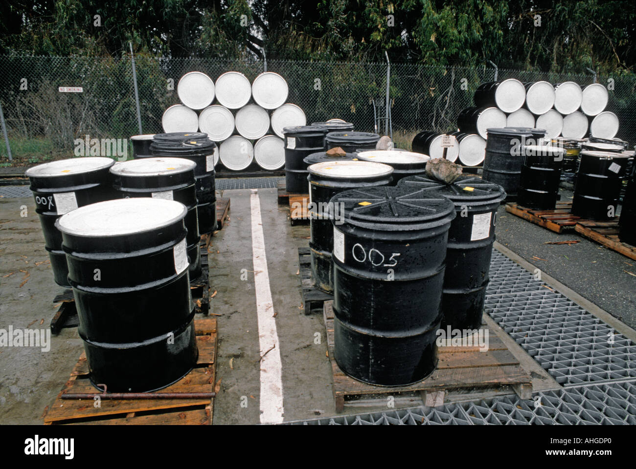 Barrels of toxic waste are lined up in a corporate yard with a sign in ...