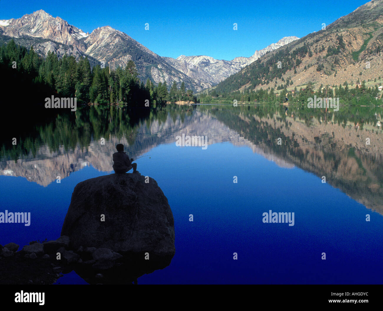 A child fishes from a boulder from the smooth lake shore in the ...