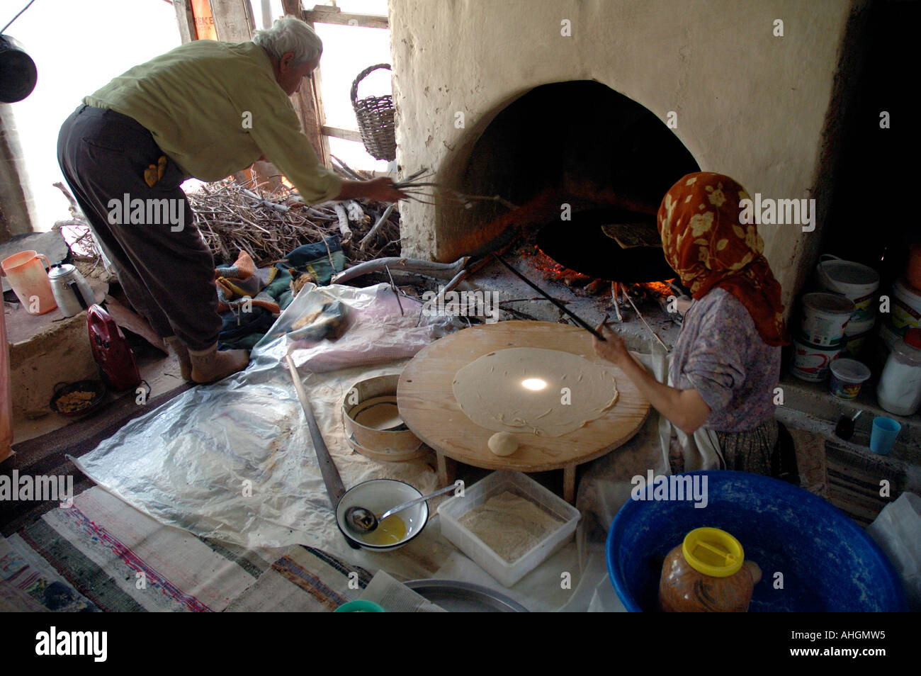 Turkish woman making flat bread in fireplace while husband stacks wood ...