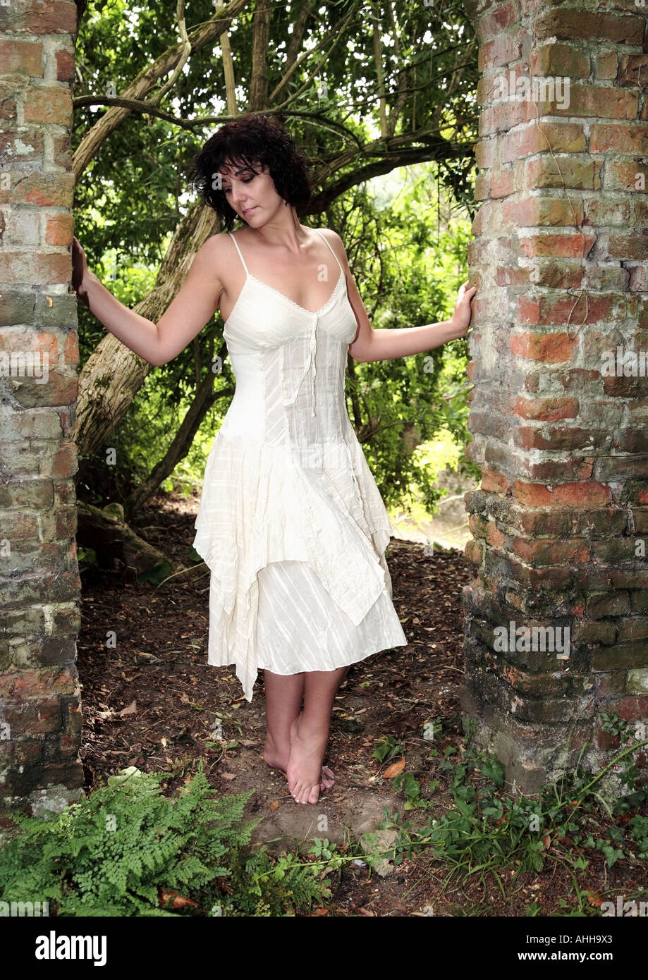 Dark haired attractive model poses barefoot at walled entrance to large ...